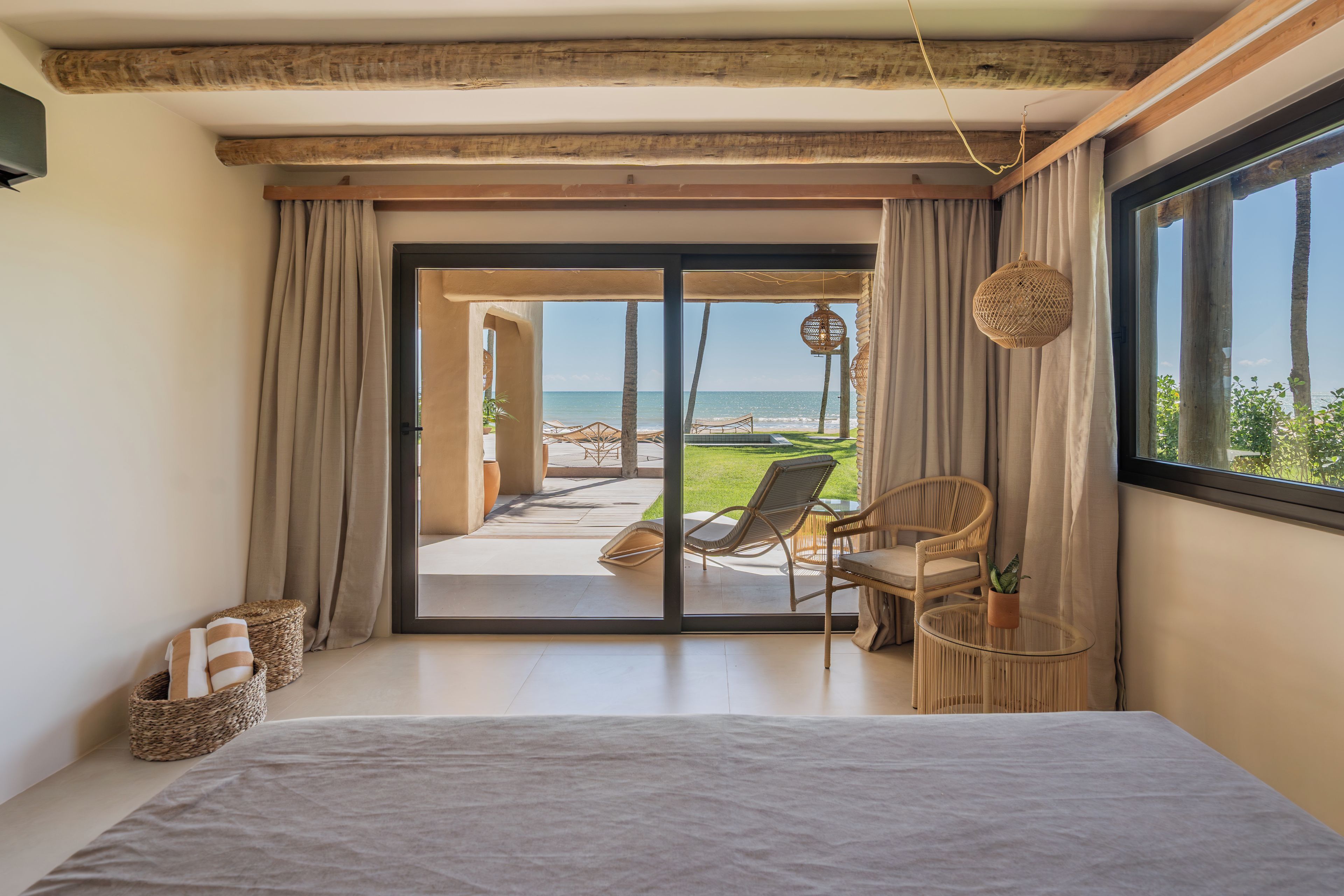 Quarto com cama grande, vista para a praia e varanda com cadeiras.
