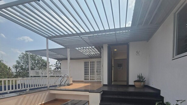 Área externa coberta com teto de vidro, escadas que levam a uma porta e vasos com plantas.