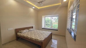 Quarto com cama, ventilador de teto, iluminação embutida, janela com vista e prateleira fixada na parede.