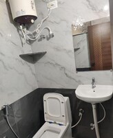 Casa de banho com sanita, lavatório e esquentador de água fixado na parede.