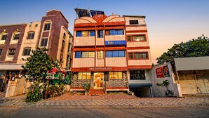 Um edifício com vários andares, um destaque com a placa 'fabHOTELS', uma escadaria que leva à entrada e uma placa de restaurante visível.