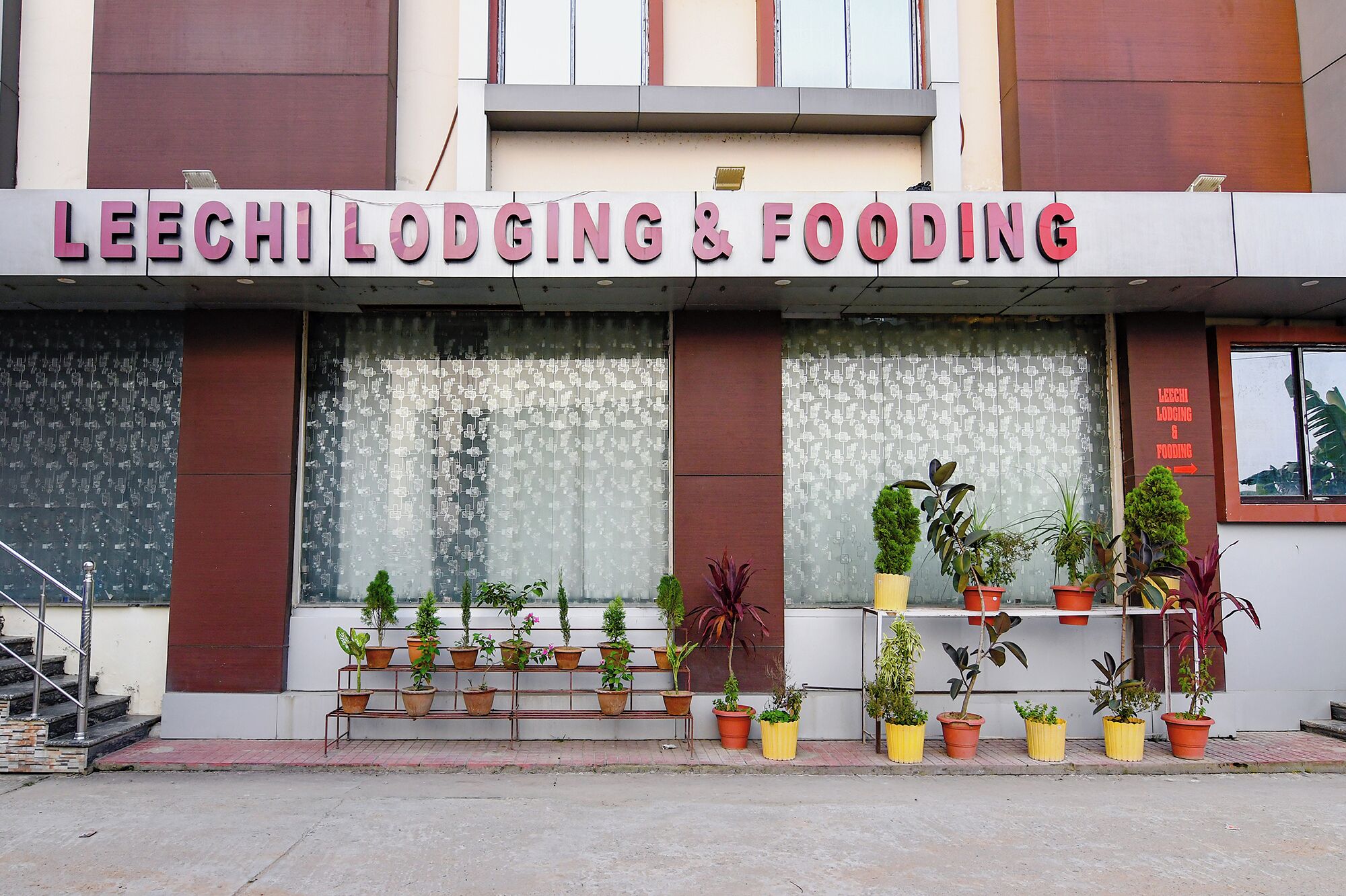 Um edifício com uma placa que diz 'LEECHI LODGING & FOODING' e vários vasos de plantas na frente.