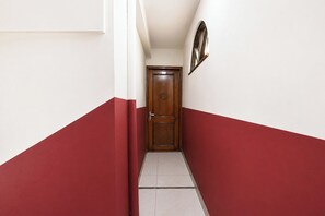Um corredor estreito com uma porta de madeira no final, paredes brancas e paredes pintadas de vermelho.