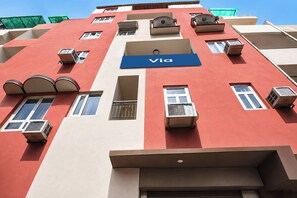 Um edifício de vários andares com fachada vermelha, um letreiro azul com a palavra 'Via', diversas varandas e aparelhos de ar condicionado.