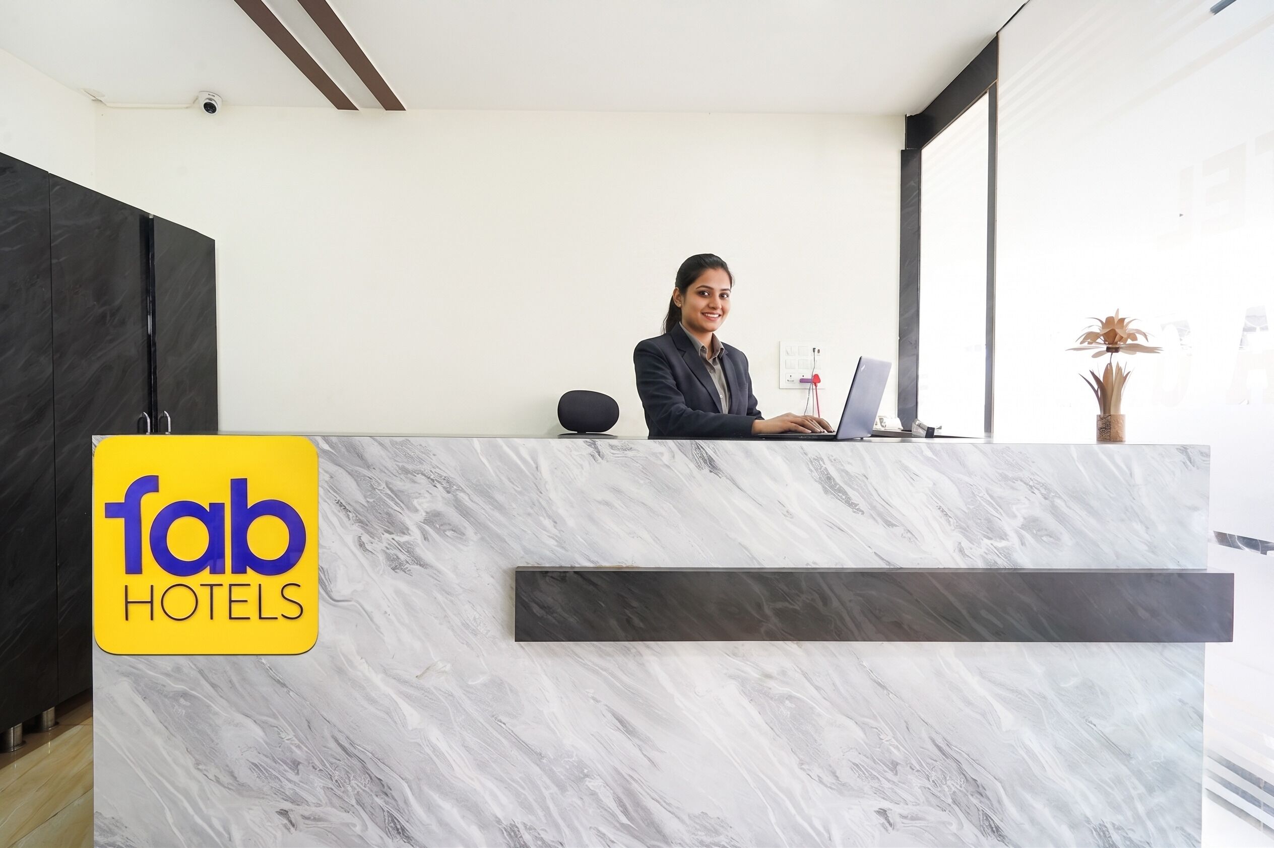Bancada de recepção com tampo de mármore, um laptop e uma placa indicando Fab Hotels.