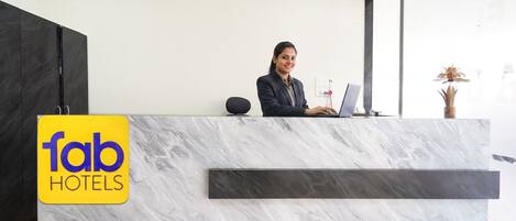 Bancada de recepção com tampo de mármore, um laptop e uma placa indicando Fab Hotels.