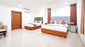Quarto de hotel com duas camas, um guarda-roupa de madeira, ventoinha no teto e janela com cortinas.