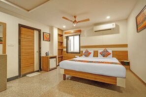 Quarto de hotel com cama, ventoinha no teto, ar condicionado, janela e porta.