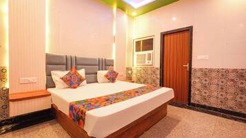Quarto de hotel com cama, mesa de cabeceira de madeira, janela com ar condicionado, porta e paredes com padrão.