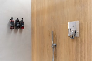 Parede de madeira com painel de controle do chuveiro e três frascos de shampoo.