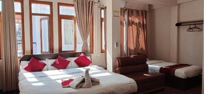 Quarto de hotel com cama, sofá, mesa pequena e janela com cortinas.