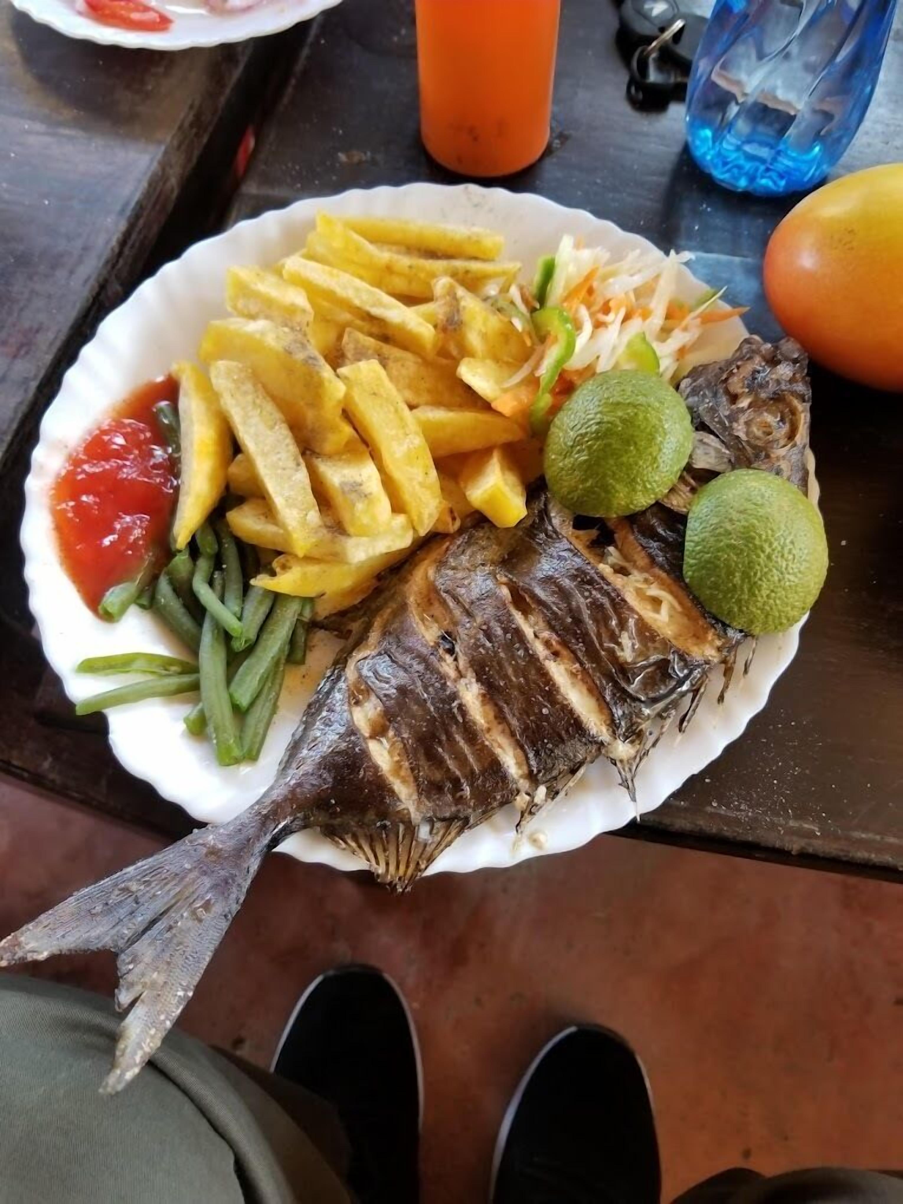 Prato com um peixe inteiro, batatas fritas, vagem e limão.