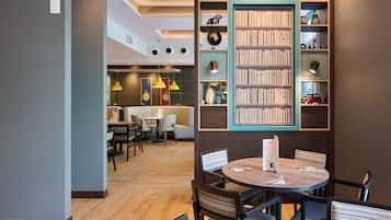 Um interior moderno com uma mesa redonda, cadeiras, uma estante de livros e uma área de jantar com mesas e cadeiras.