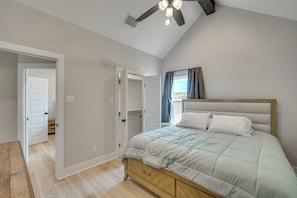 Quarto com cama, ventilador de teto e janela com cortinas.