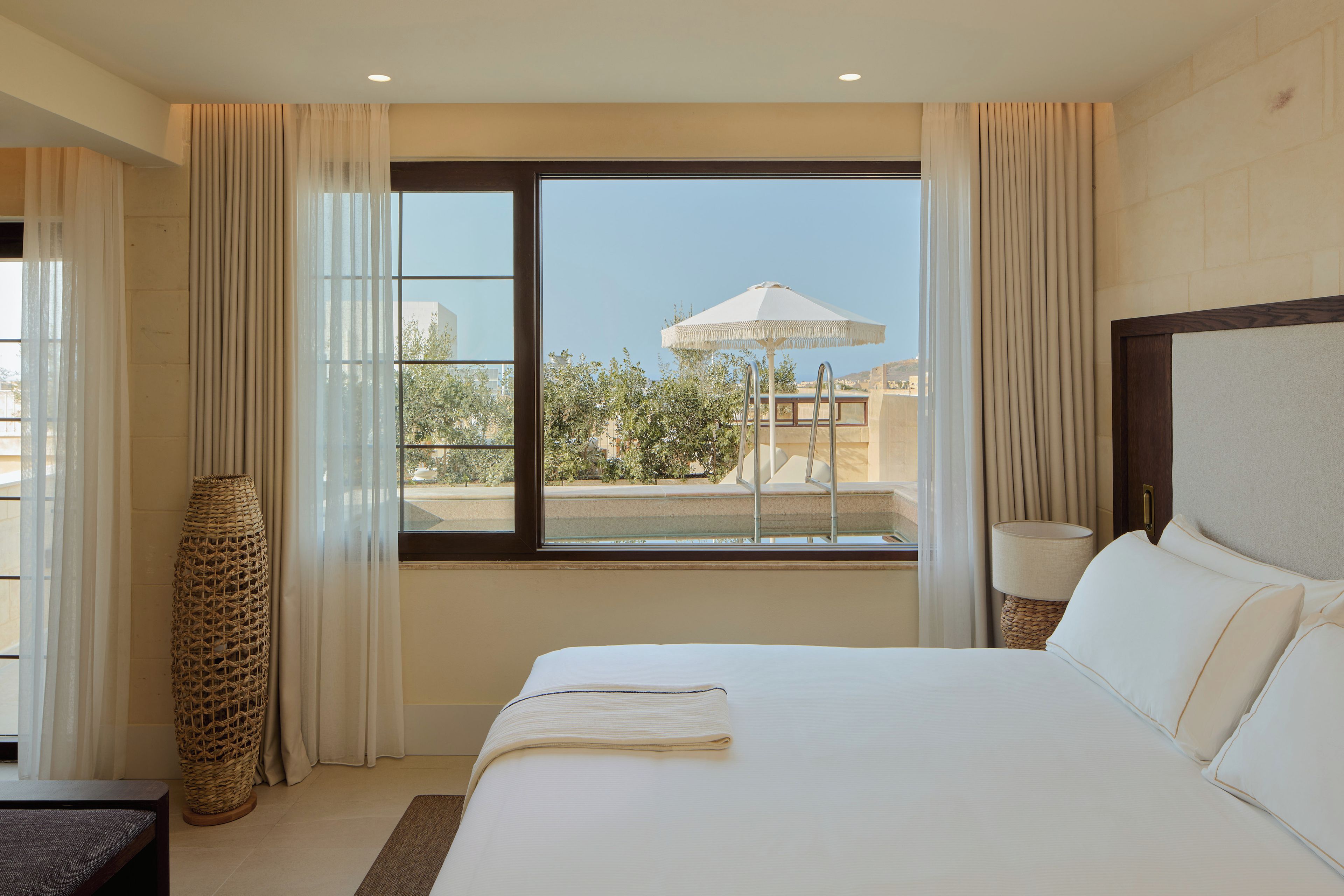 Quarto de hotel com uma cama grande, vista para a paisagem urbana e varanda com guarda-sol.