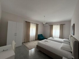 Quarto de hotel moderno com duas camas, uma mesa de trabalho, uma cadeira e um pequeno espaço de estar.
