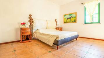 Um quarto com uma cama, mesa de cabeceira, abajur, quadro e janela com cortinas.
