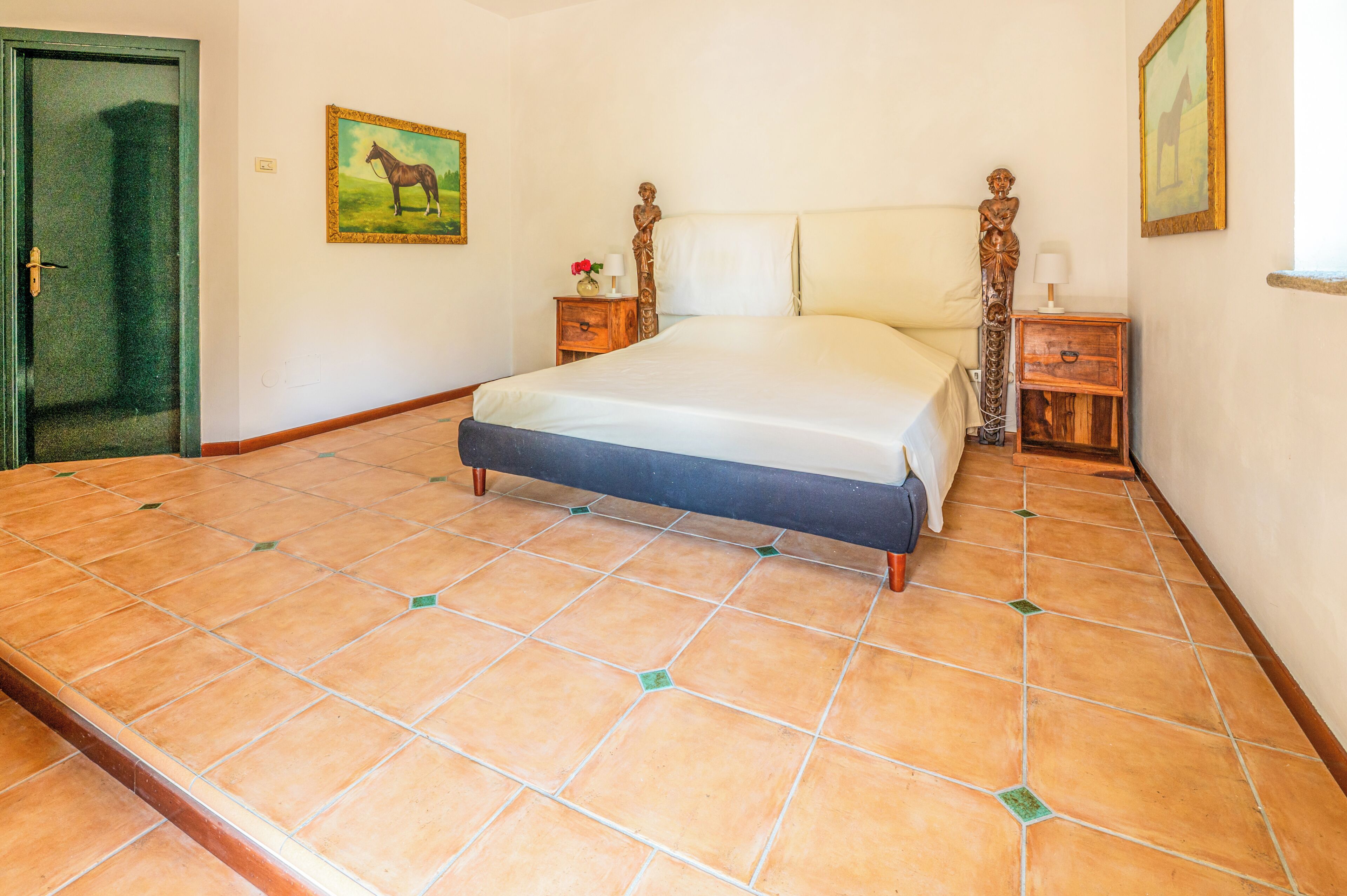 Quarto com cama, mesa de cabeceira, luminária na parede e uma porta.