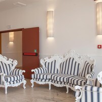 Uma área de estar com poltronas e sofás estofados com listras, uma porta de madeira e luminárias fixadas na parede.