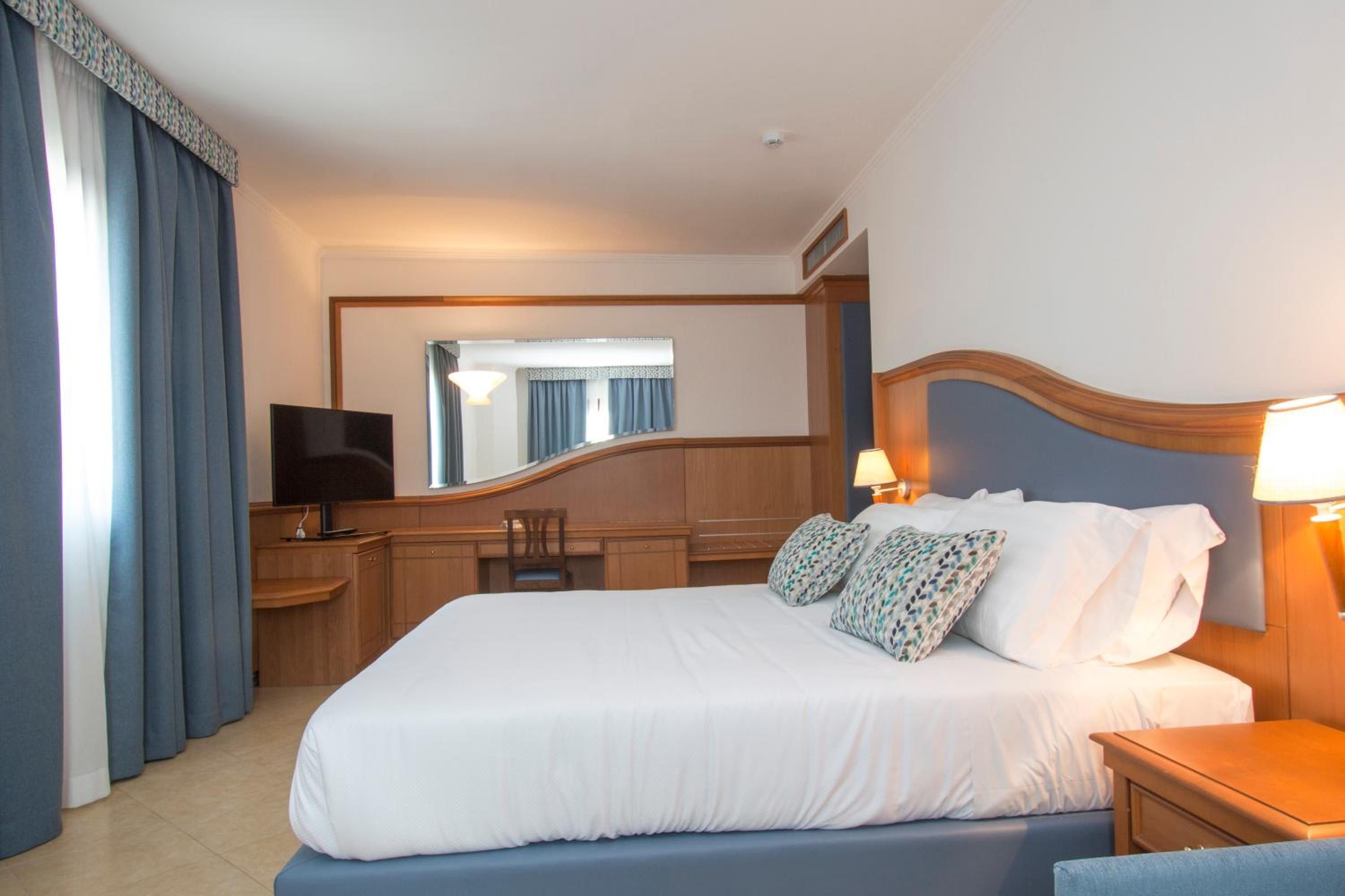 Quarto de hotel com uma cama grande, uma escrivaninha com televisão e um espelho.