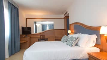 Quarto de hotel com uma cama grande, uma escrivaninha com televisão e um espelho.