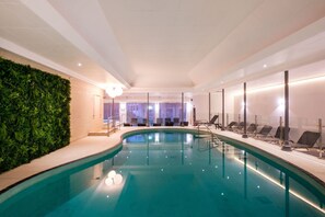 Piscina com parede verde e cadeiras de descanso.