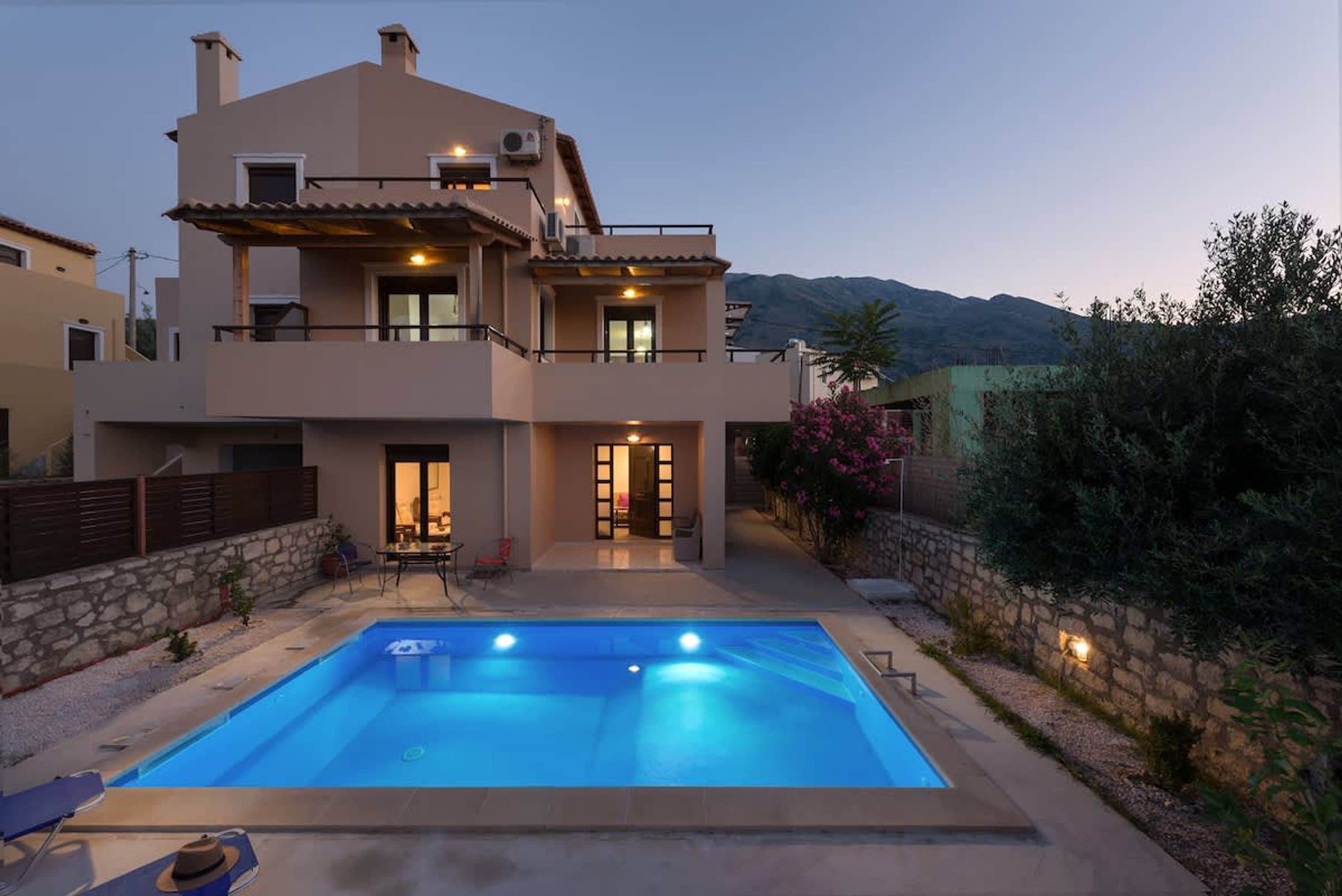 Uma casa de dois andares com piscina, paredes de pedra e vista para montanhas.