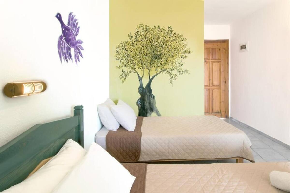 Quarto com duas camas, uma luminária na parede e um mural de uma árvore.