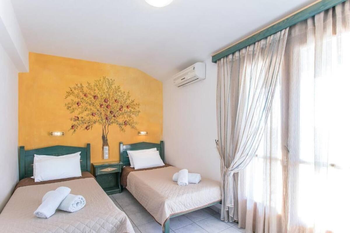 Quarto de hotel com duas camas, um quadro de uma árvore, ar condicionado e uma janela com cortinas.