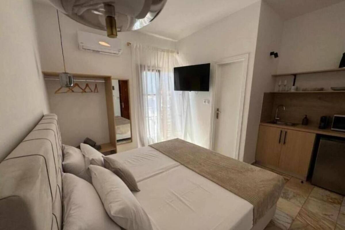 Quarto de hotel com cama, televisão na parede, cozinha compacta e banheiro visível por uma porta aberta.