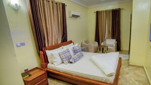 Quarto de hotel com cama de madeira, mesa de cabeceira, cadeira e escrivaninha.