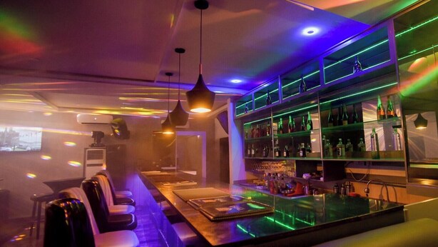 Uma área de bar com um balcão comprido, banquetas e prateleiras cheias de garrafas.