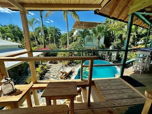 Um deck de madeira com piscina, palmeiras e uma casa ao fundo.
