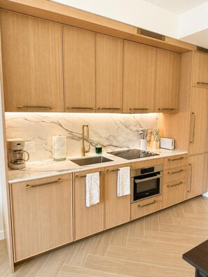 Cozinha moderna com armários de madeira, bancada de mármore, pia, cafeteira, torradeira e forno.