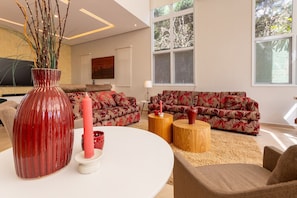 Uma sala de estar moderna com um vaso vermelho, dois sofás, uma mesa redonda e uma janela ampla.