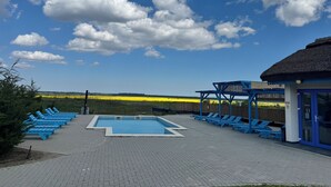 Uma área de piscina com espreguiçadeiras azuis, uma piscina e um edifício com telhado de palha.
