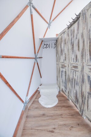Um quarto com parede branca, piso de madeira, objeto circular branco e um armário rústico de madeira.