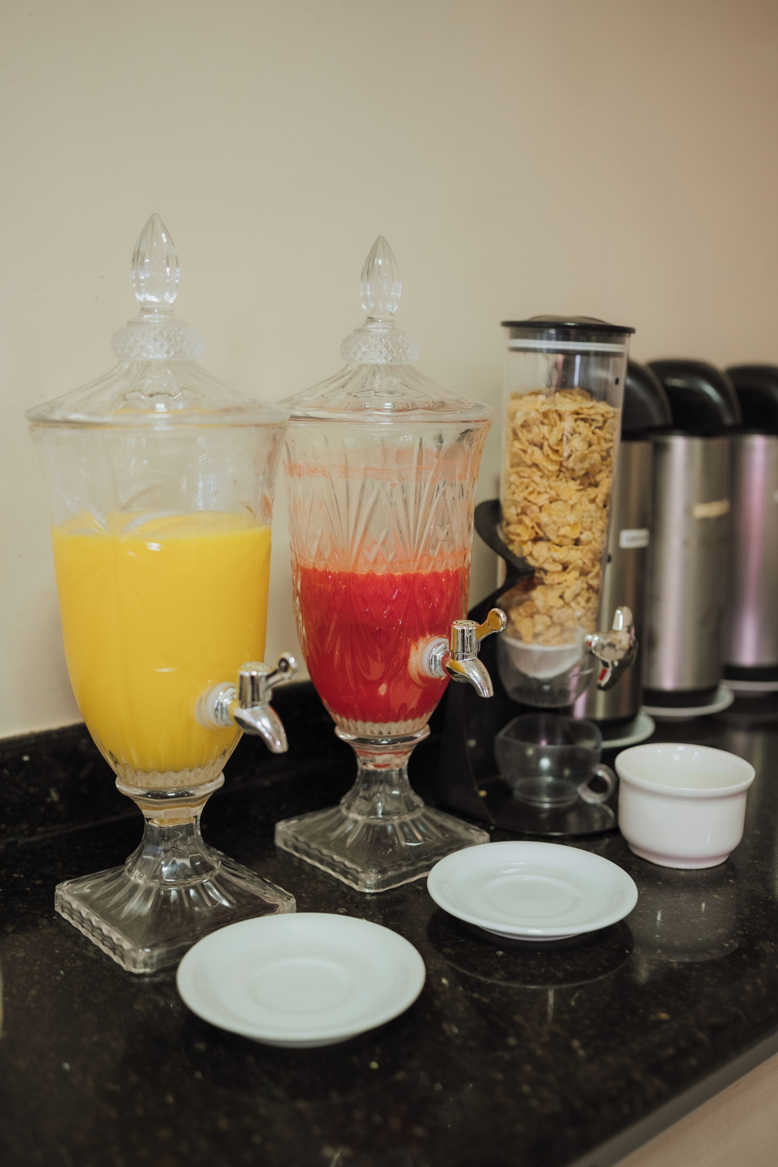 Dois distribuidores de bebidas com recipientes transparentes, um recipiente com granola e uma cafeteira em uma bancada de cozinha.