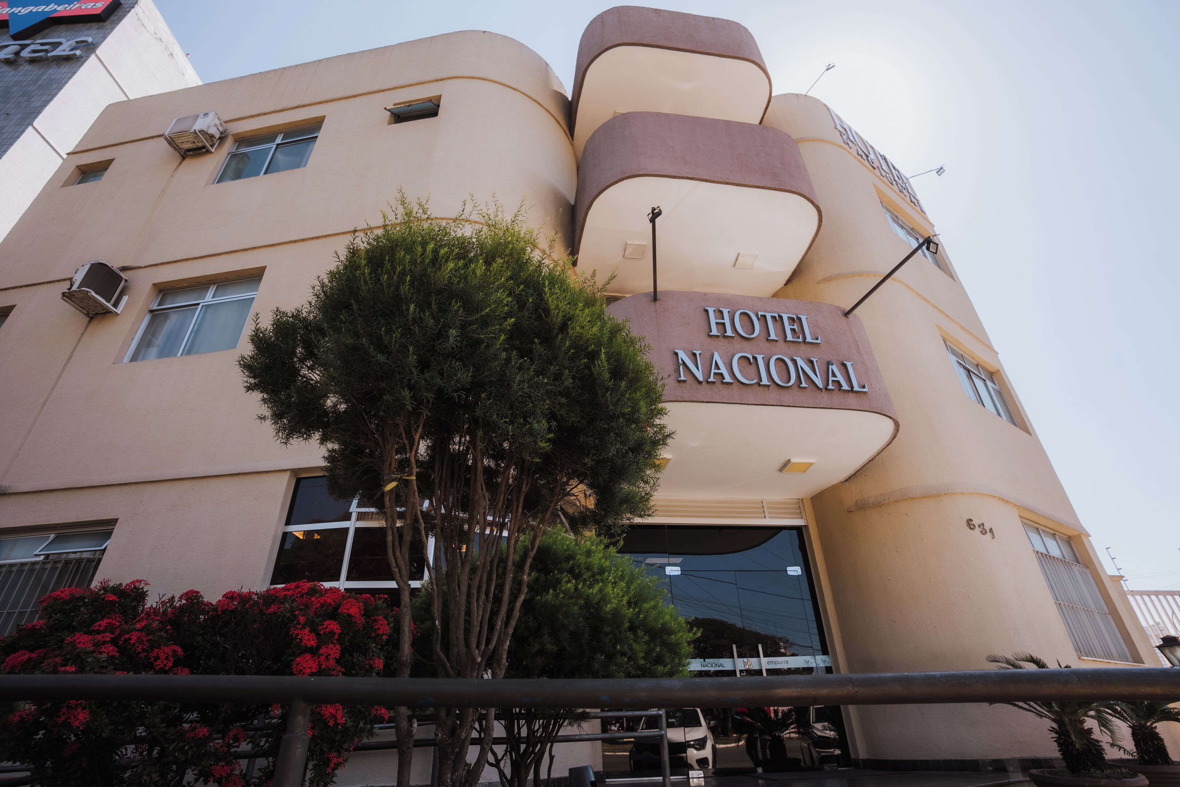 Um edifício de hotel com fachada curva, uma placa com a inscrição 'HOTEL NACIONAL' e uma árvore na frente.