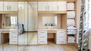 Quarto moderno com um espelho grande, uma escrivaninha e um guarda-roupa com vários compartimentos.