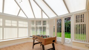 Quarto com mesa de futebol, janelas amplas e vista para um jardim.