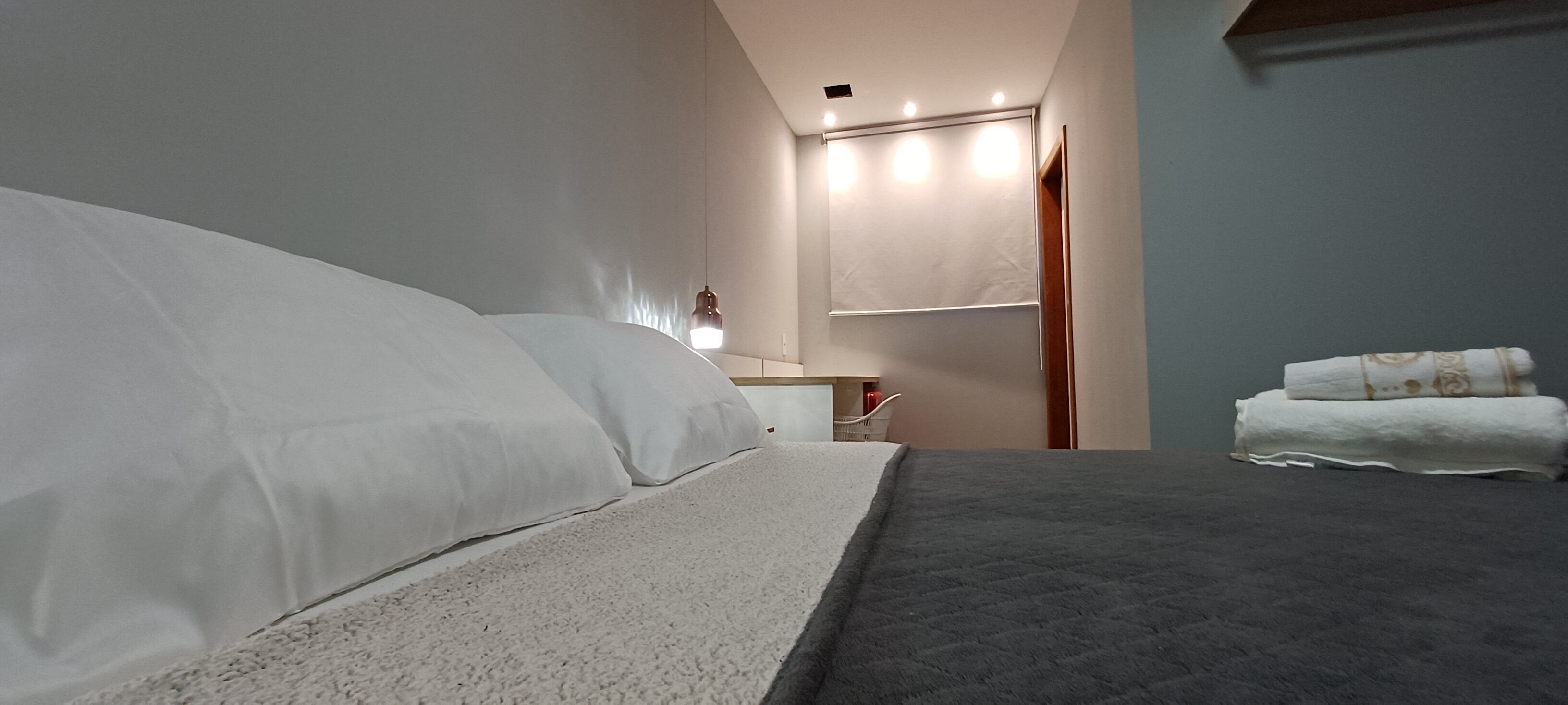 Quarto com cama, mesa de cabeceira, espelho e porta-toalhas.