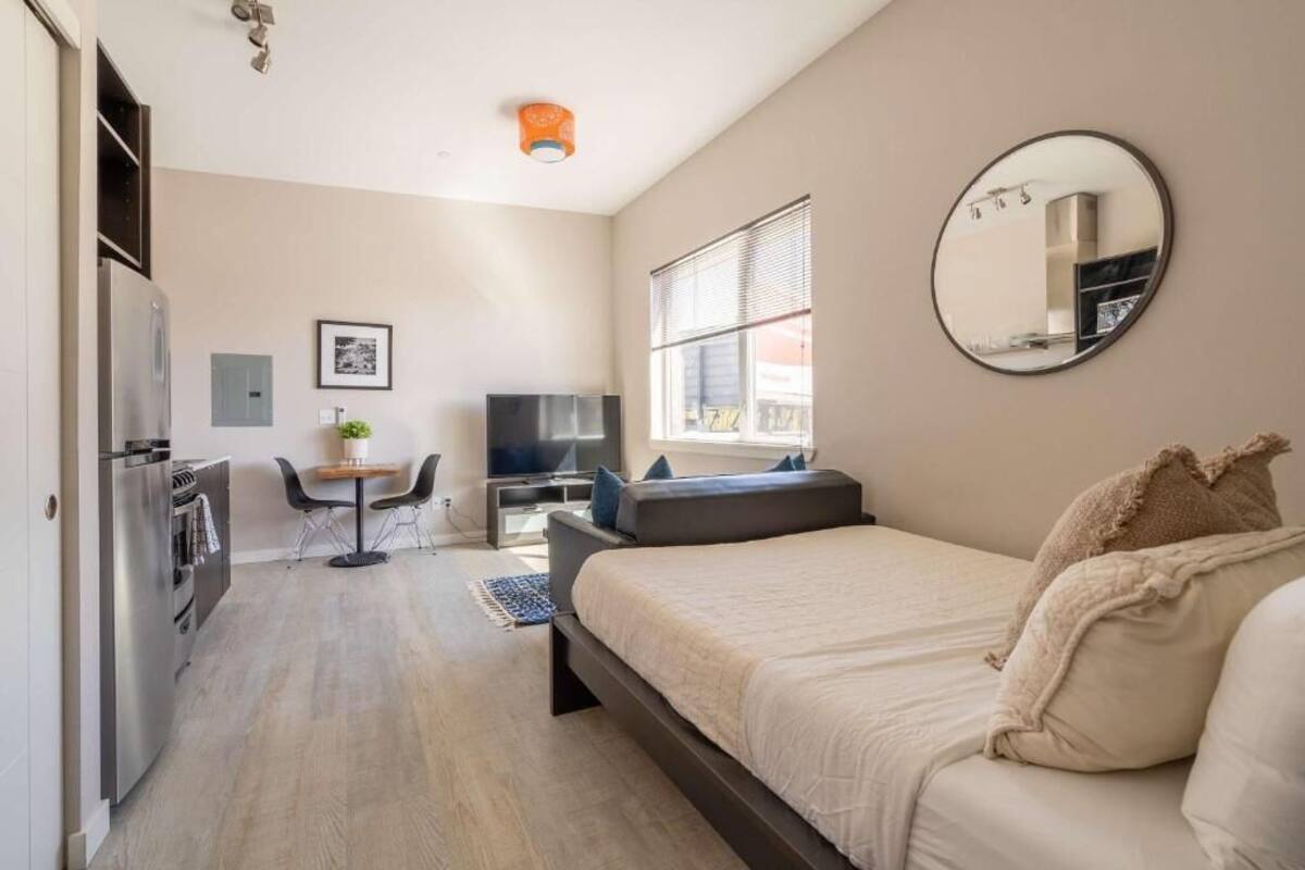 Quarto moderno com cama, televisão, secretária e kitchenette.