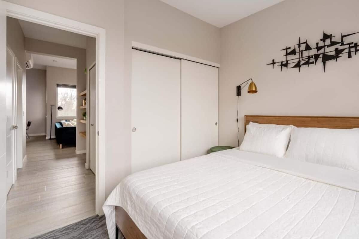 Quarto com cama, guarda-roupa, mesa de cabeceira, luminária e uma obra de arte na parede.