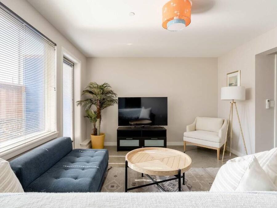 Uma sala de estar moderna com um sofá, uma mesa de centro redonda de madeira, uma televisão, uma planta em vaso e um abajur.