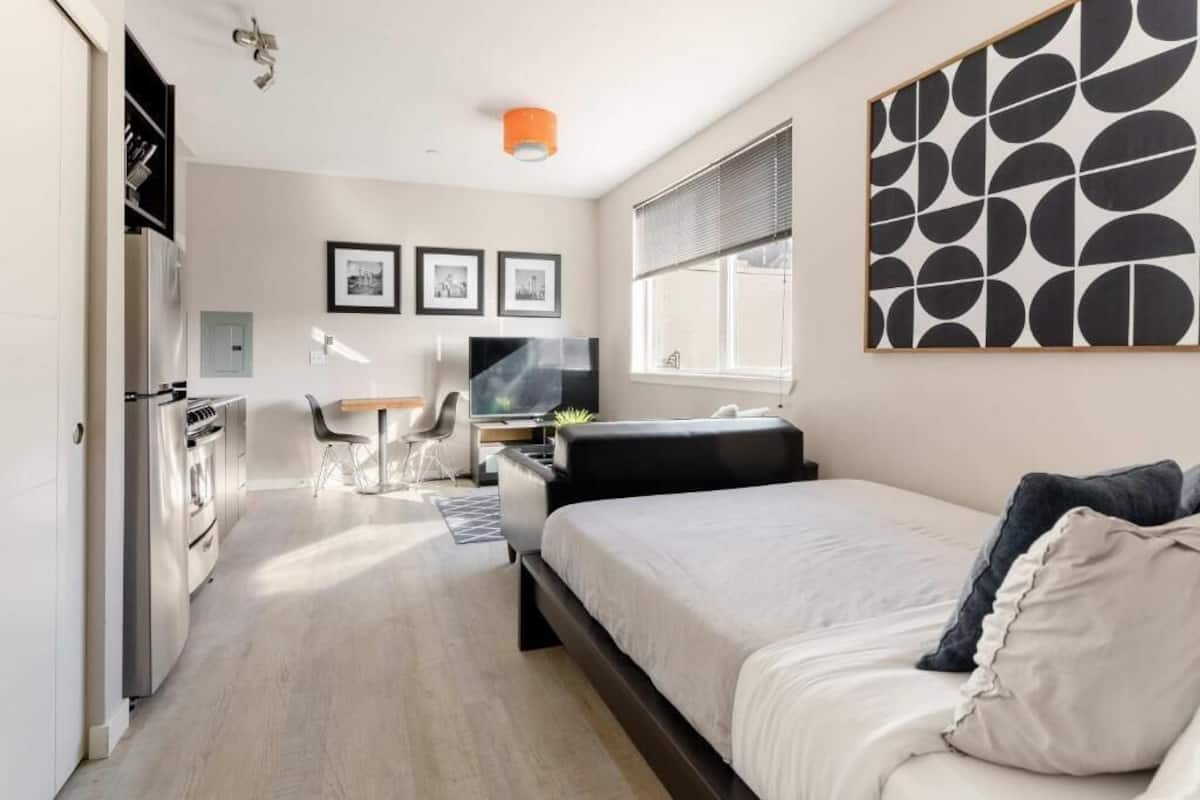 Quarto de hotel moderno com cama, escrivaninha e kitchenette.