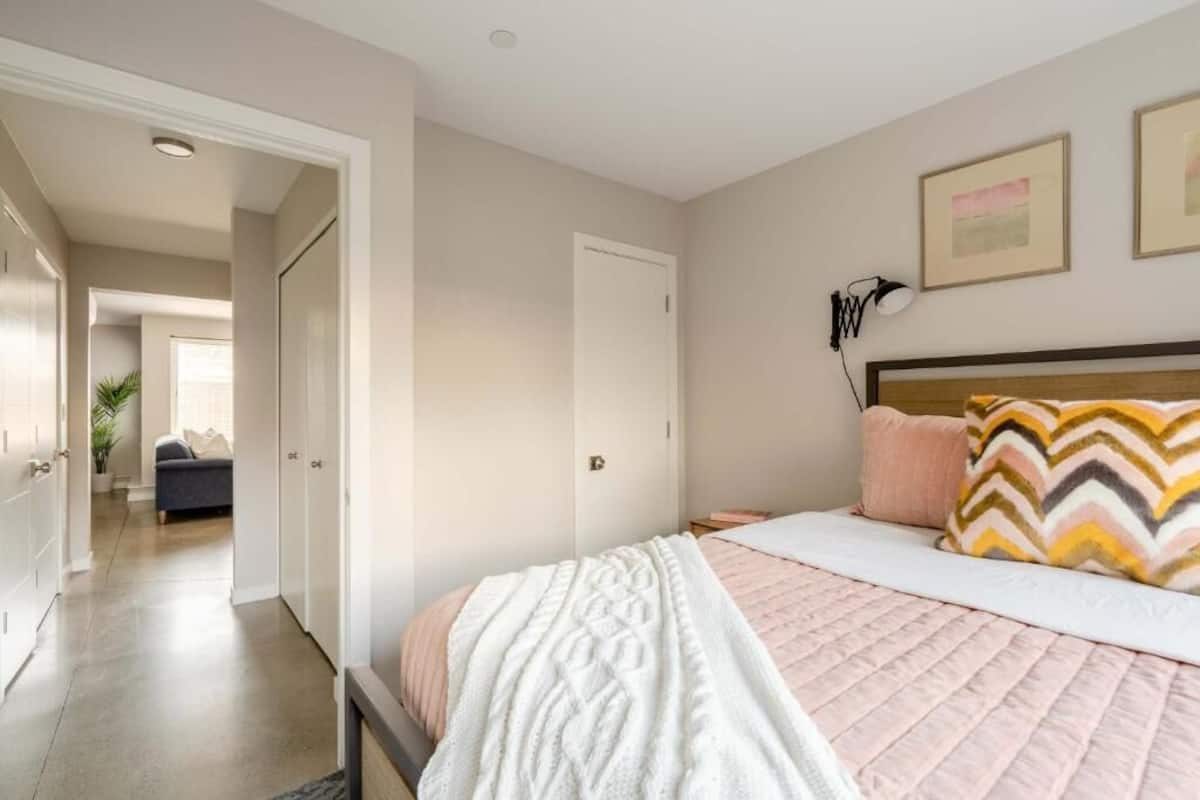 Um quarto com uma cama, mesa de cabeceira, abajur e porta.