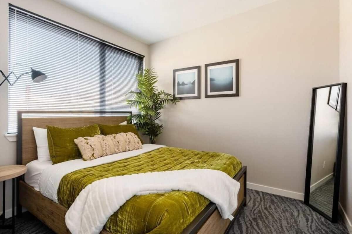 Quarto bem arrumado com cama, mesa de cabeceira, abajur e quadros nas paredes.