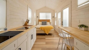 Quarto compacto e moderno com cama, pequena cozinha e área de refeições.