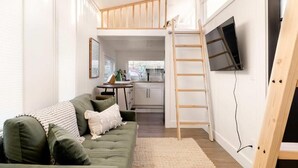 Um espaço compacto com quarto no mezanino, cozinha compacta e televisão na parede.